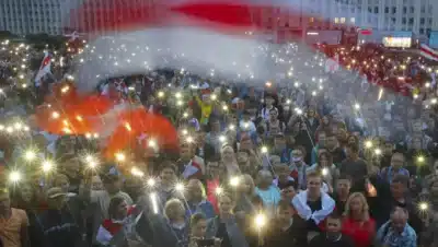 A mass protest in Minsk with thousands of Belarusians holding phone lights and waving the white-red-white opposition flag, symbolizing peaceful resistance against dictatorship in Belarus.